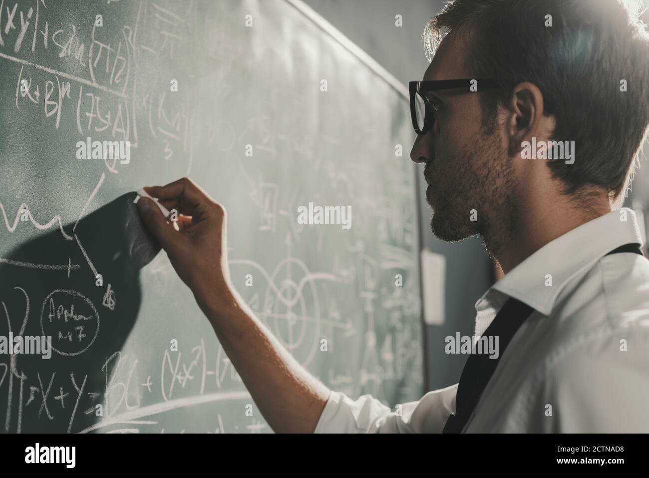 Young smart mathematician drawing math formulas on the chalkboard and ...