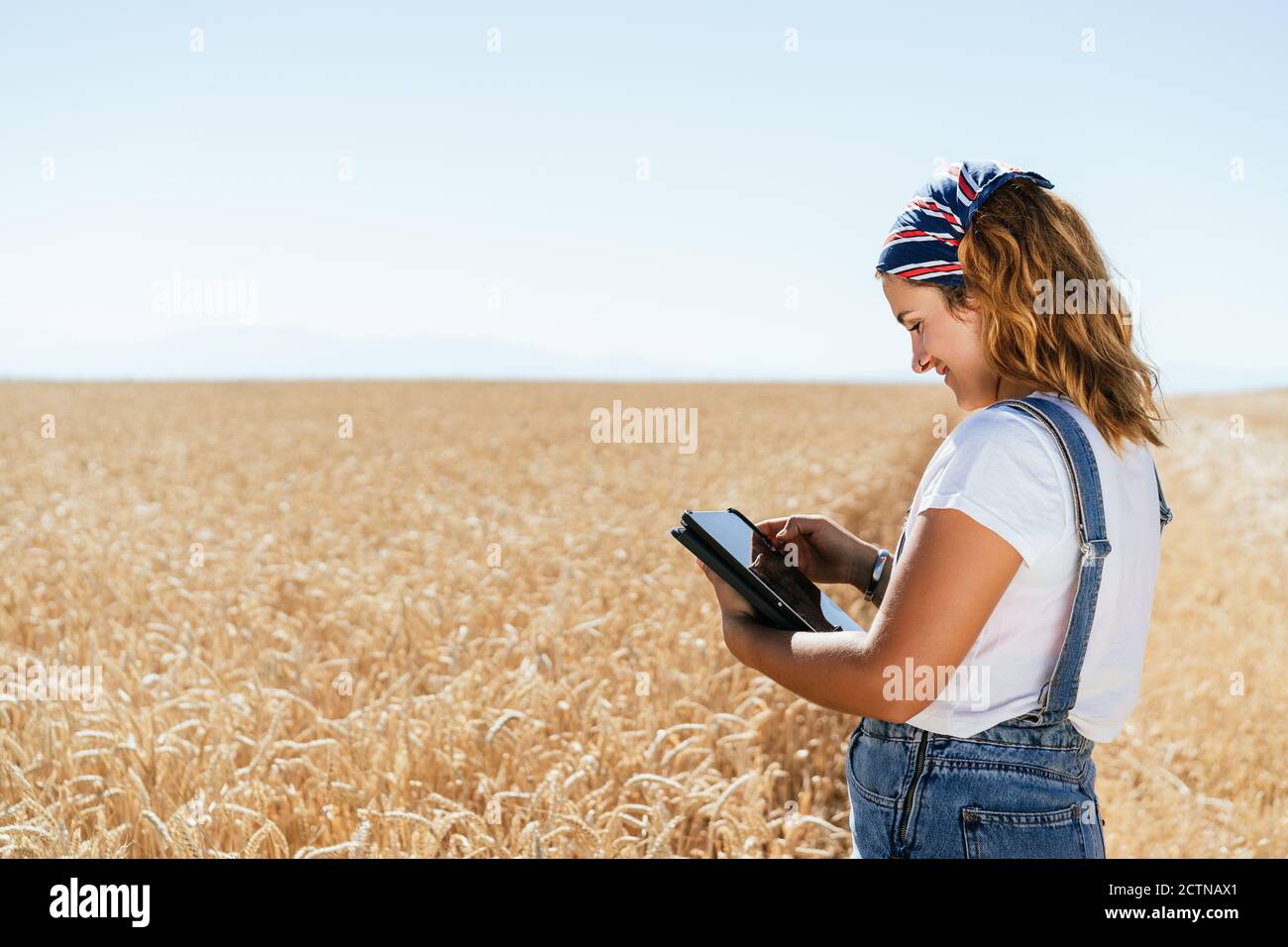 Side view of positive focused female farmer in overalls standing in ...