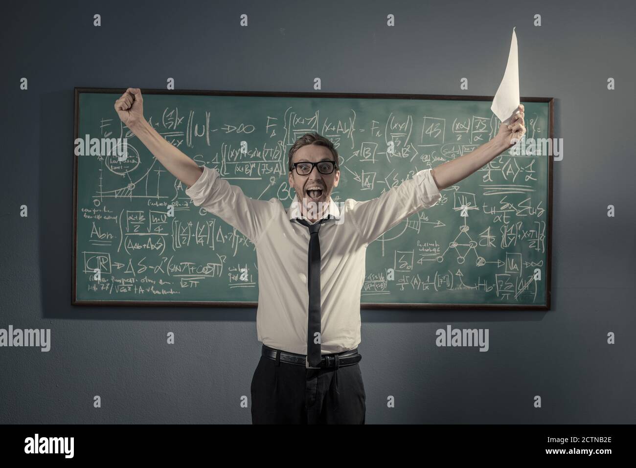 Cheerful successful mathematician standing in front of a chalkboard ...