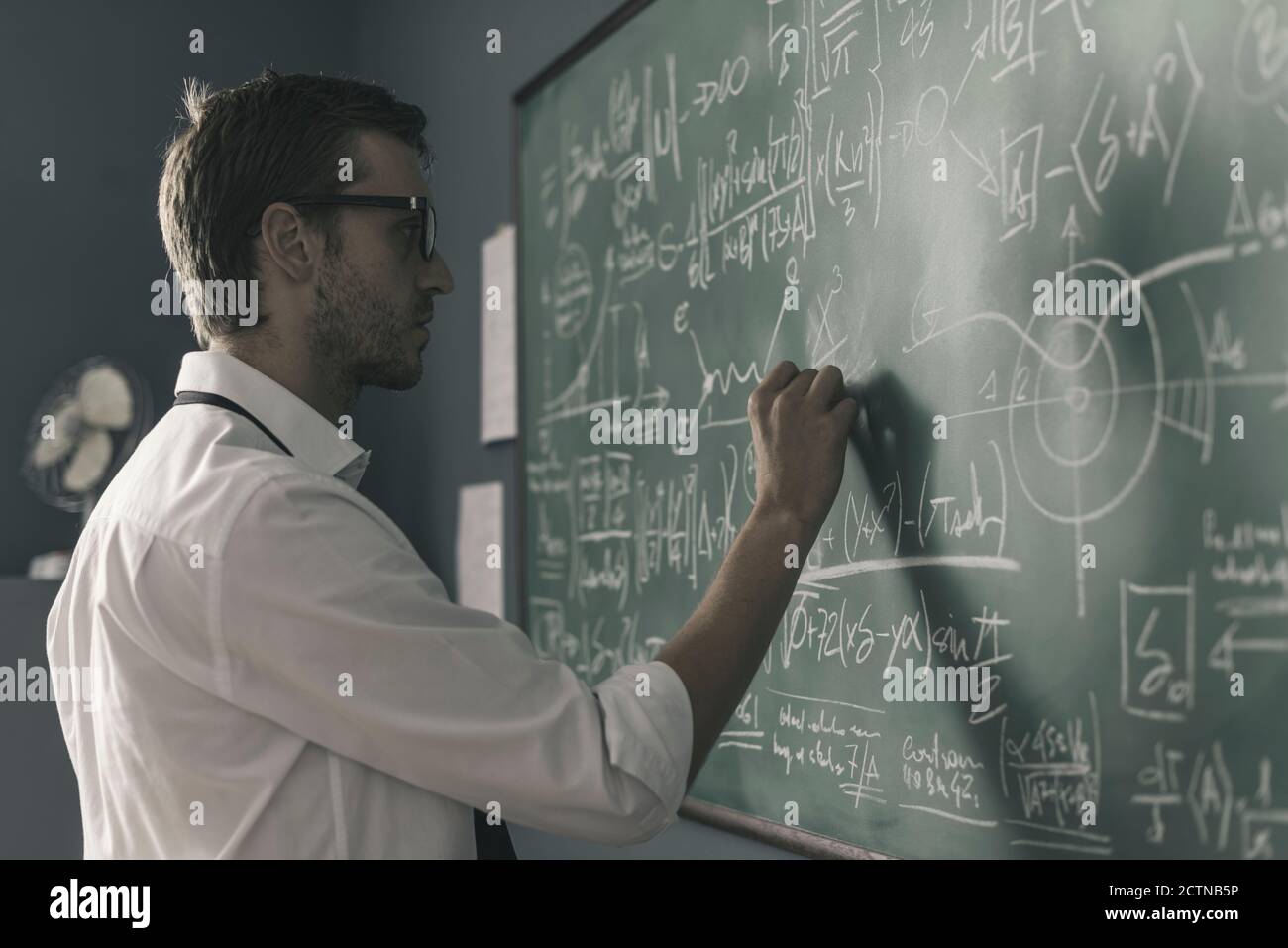 Young smart mathematician drawing math formulas on the chalkboard and ...