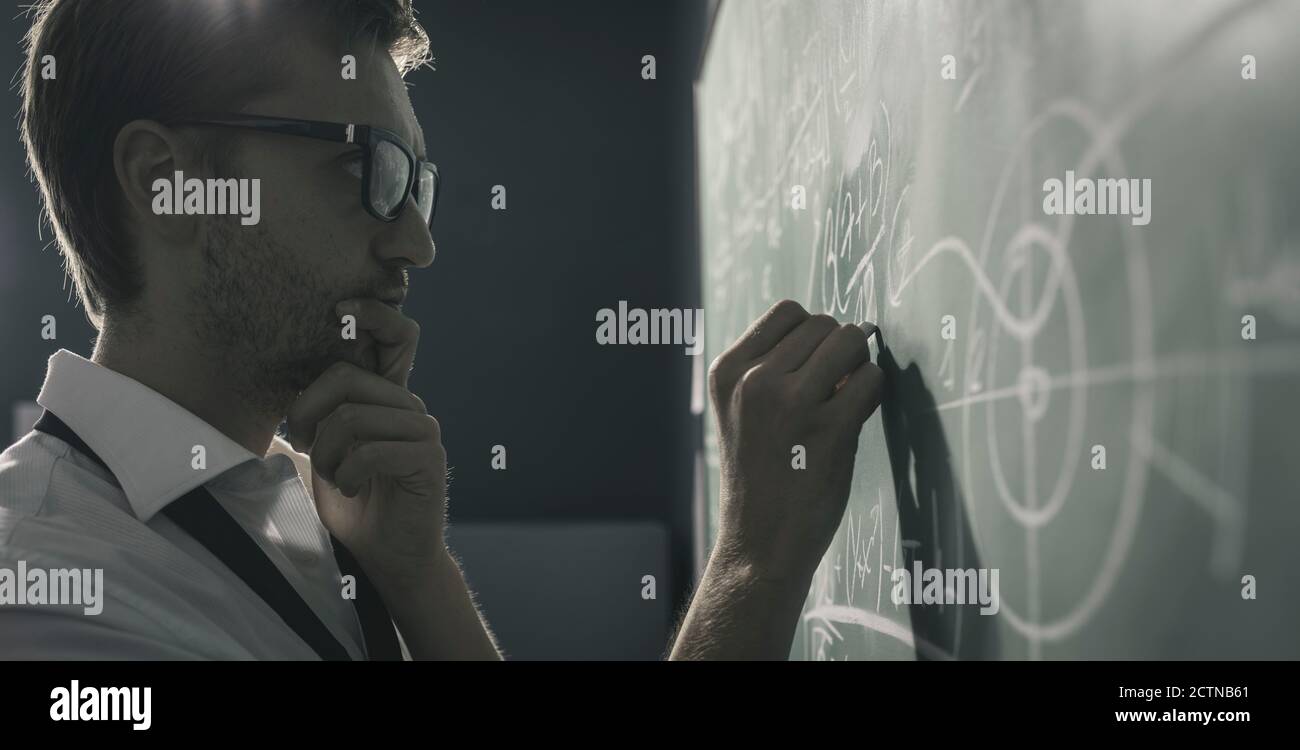 Young smart mathematician drawing math formulas on the chalkboard and ...