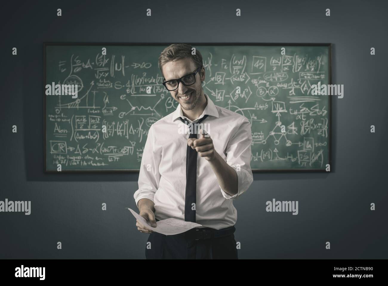 Confident smiling professor standing in front of a chalkboard with math ...