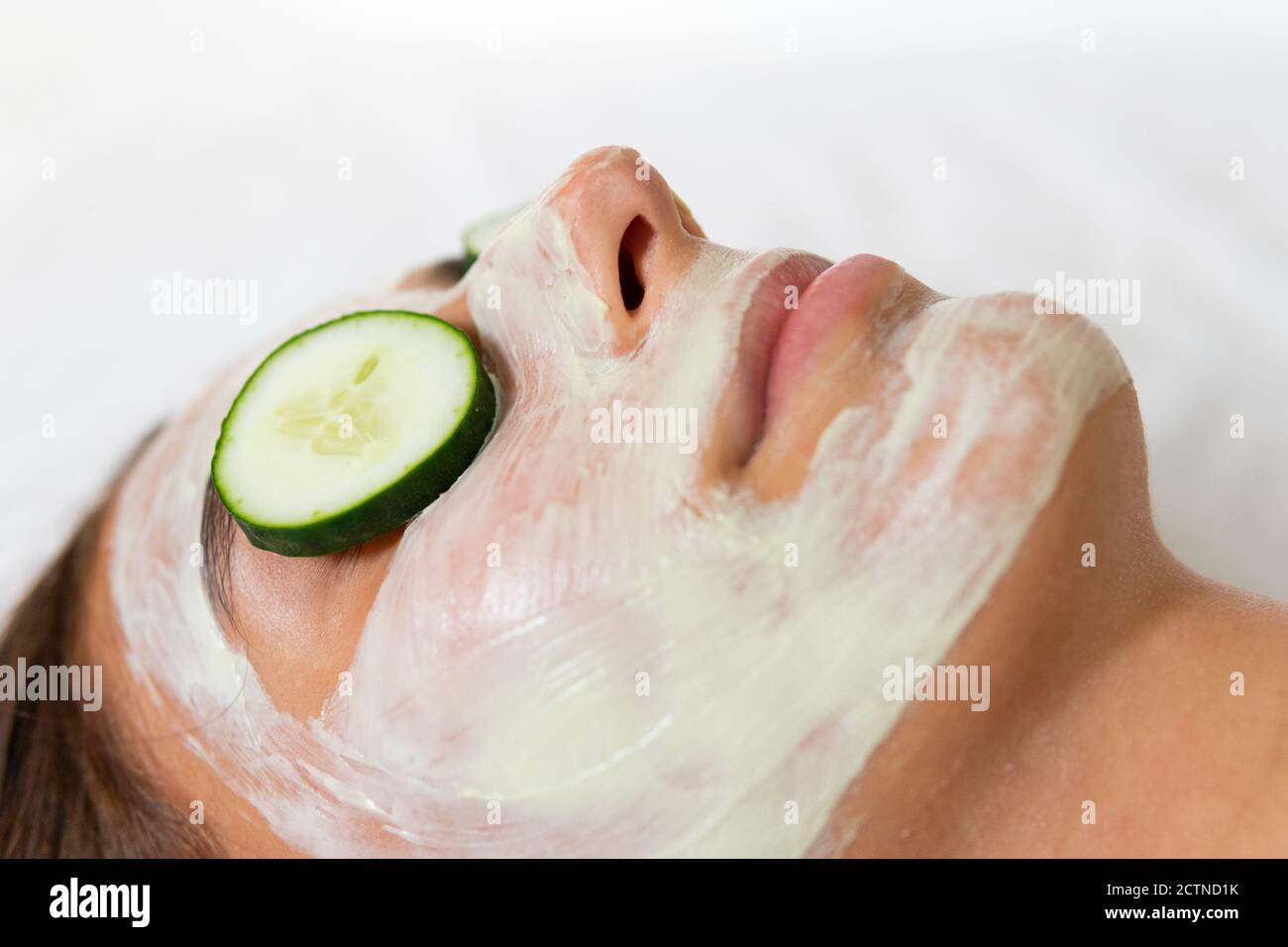 Closeup of relaxed female with hydrating facial mask and slices of fresh cucumber on eyes ...