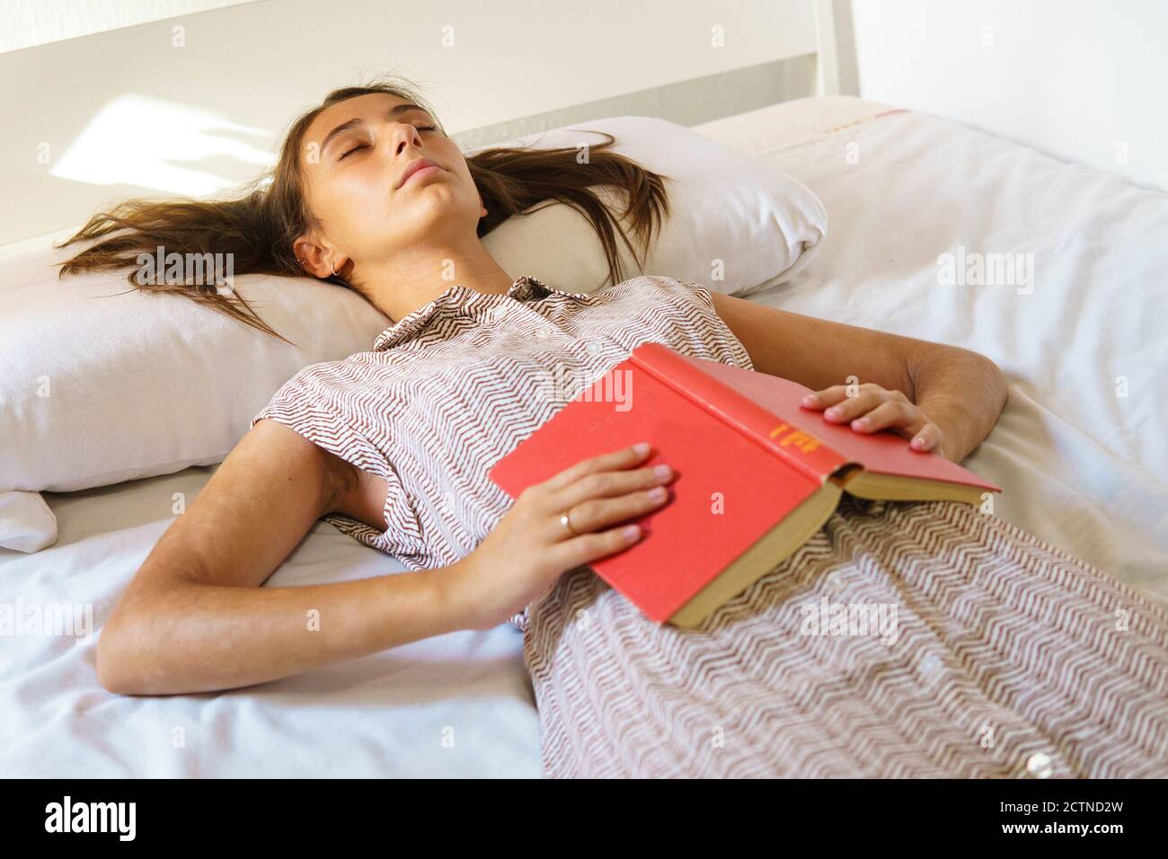 Young female falling asleep with book while lying on comfortable bed at ...