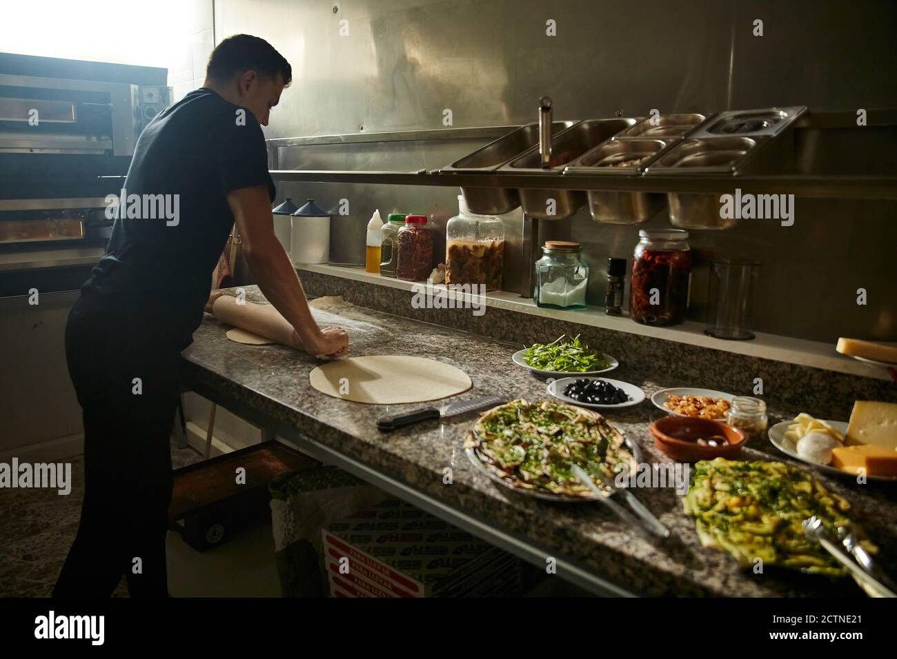 Side view of man using rolling pin to stretch fresh dough on on marble ...