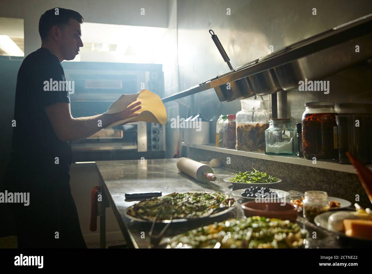 Side view of man flipping and tossing dough on table with flour while ...