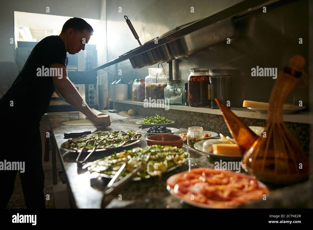 Side view of man using rolling pin to stretch fresh dough on on marble ...