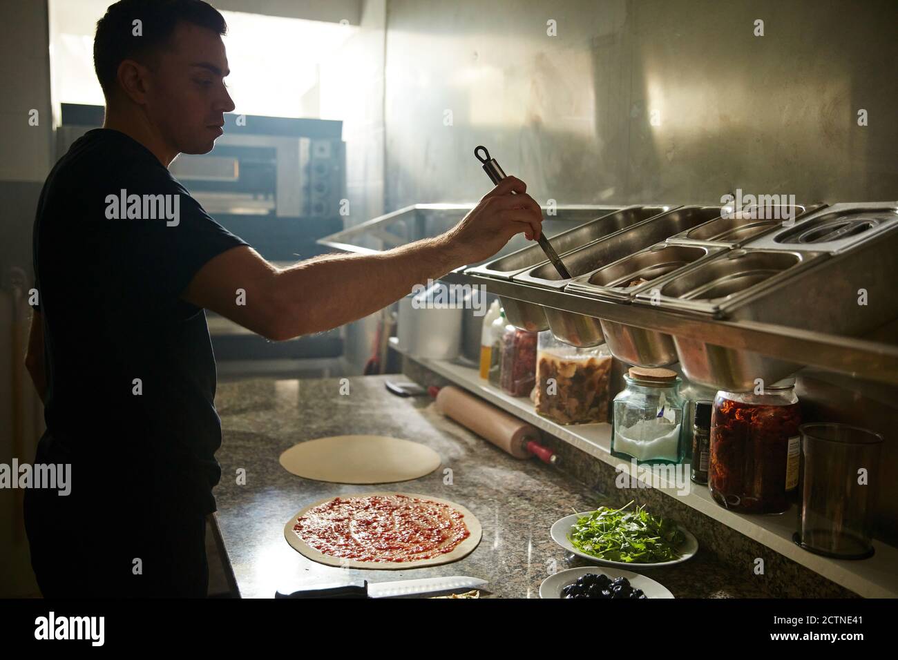 Side view of chef pouring and spreading tomato sauce on dough with ...