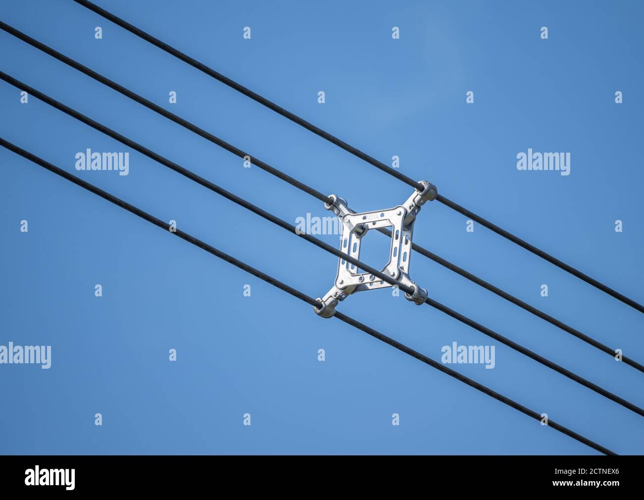 a four way metal power line spacer, grey with a blue sky background ...