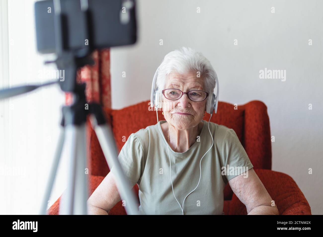 Content senior lady in headphones sitting in cozy armchair at home and ...