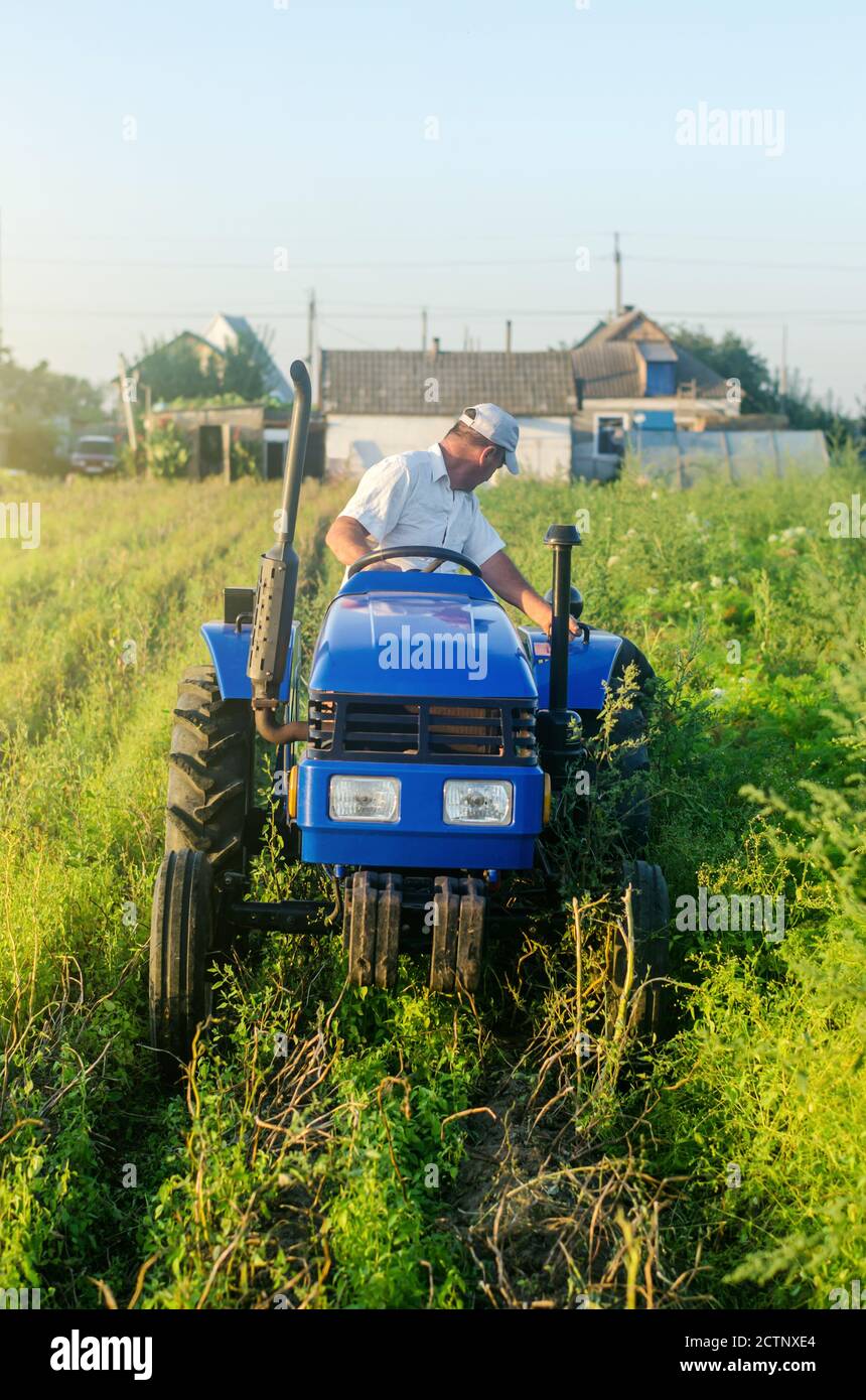 A farmer on a tractor drives across the farm field and harvests ...