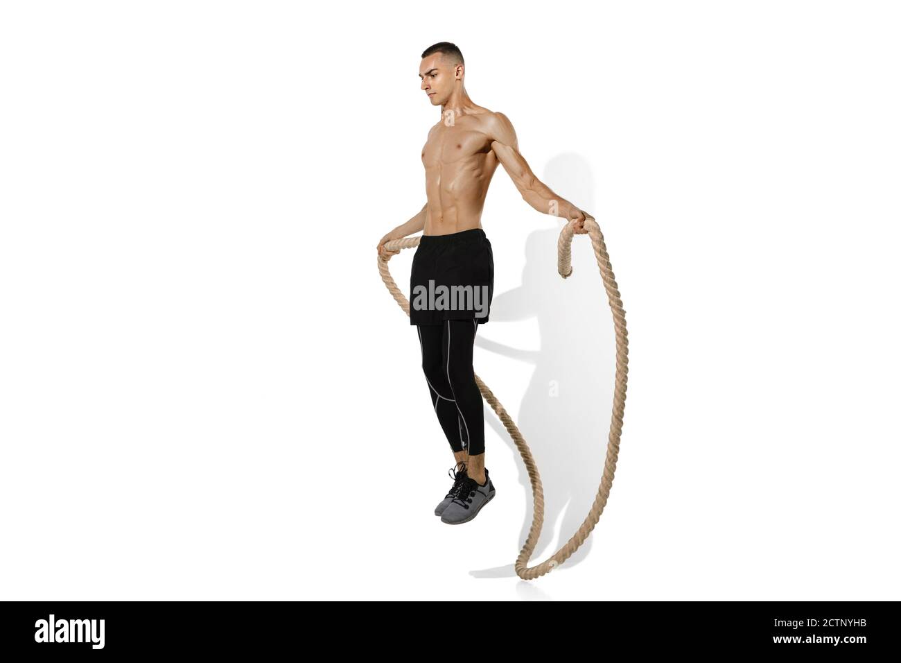Jumping with rope. Stylish young male athlete practicing on white ...