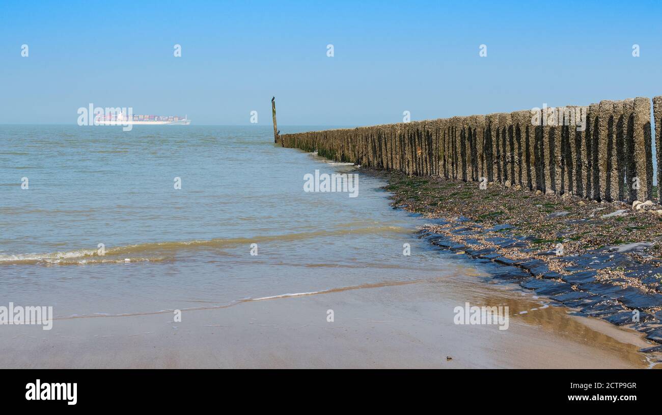A breakwater made of wooden poles covered by barnacles and of stones at ...