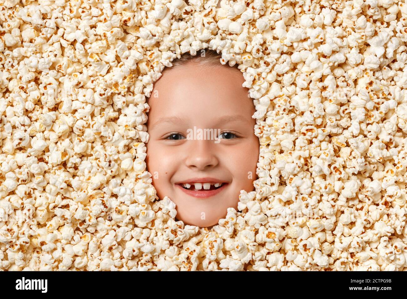 Cute happy pretty little girl face in popcorn. Top view of the child ...