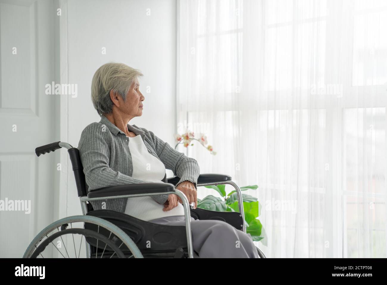 Rear view of a senior woman sitting on wheelchair looking outside the ...