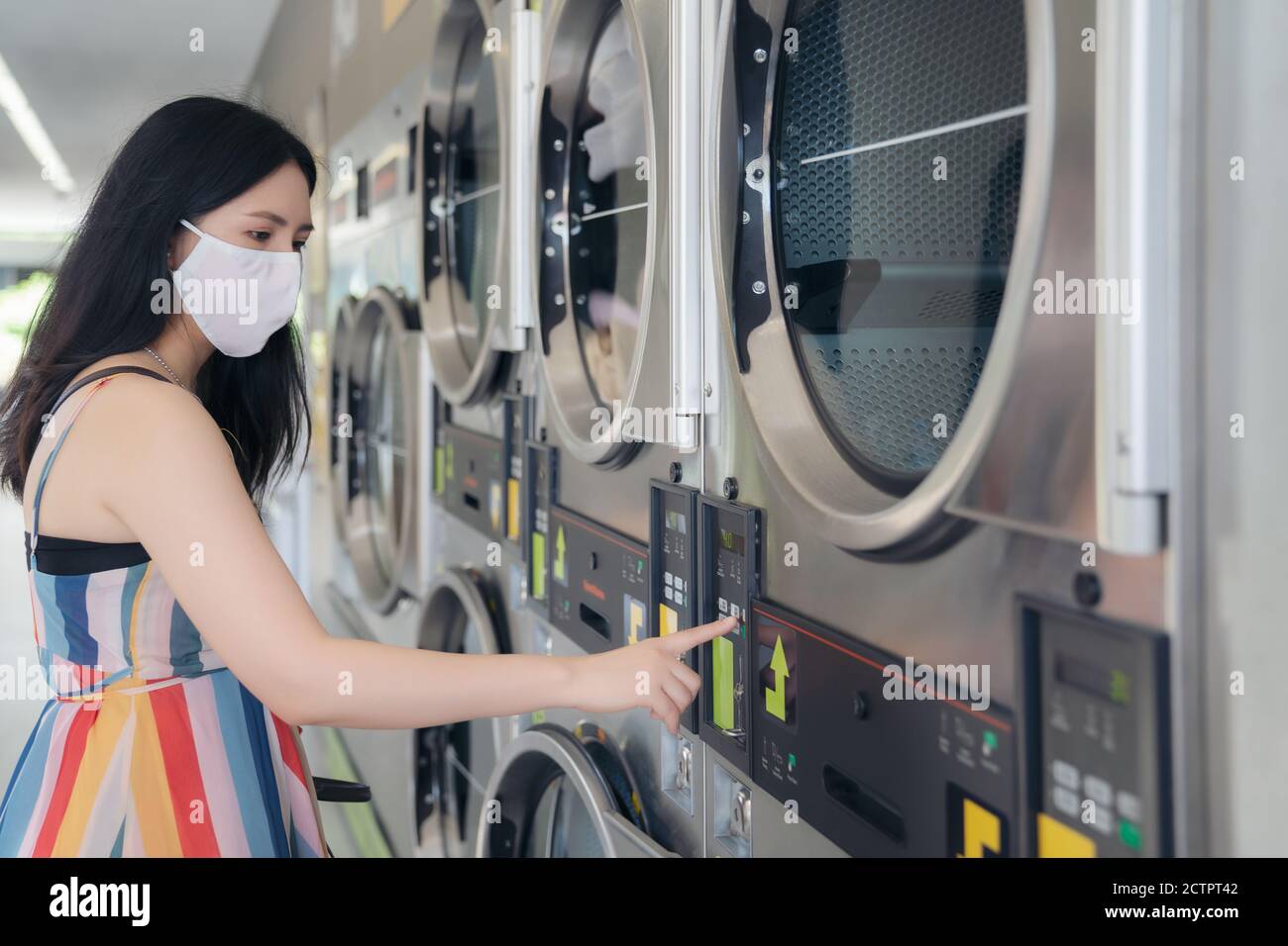 Beautiful woman with mask doing laundry at laundromat shop Stock Photo ...