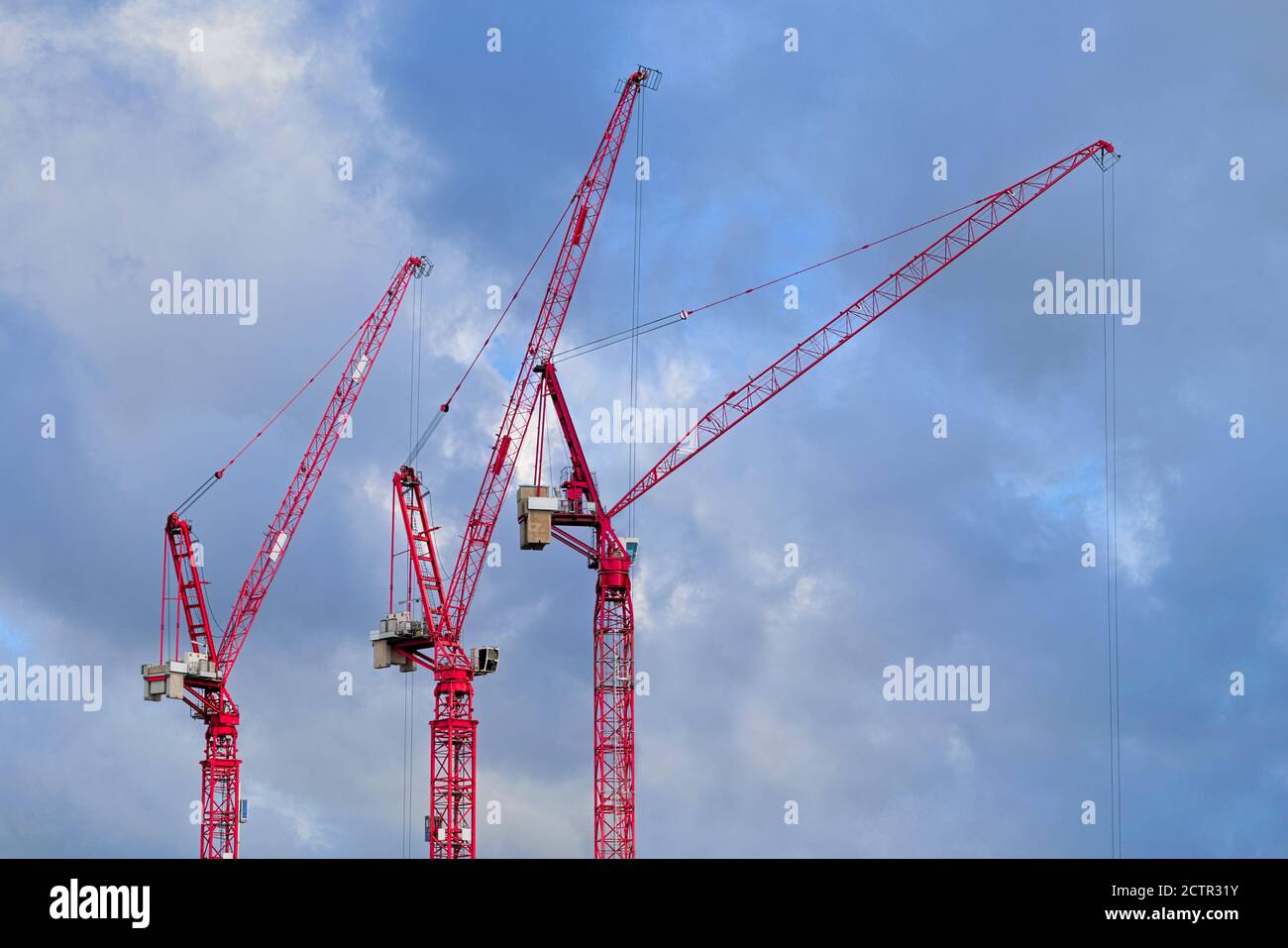 Three red tower cranes, cloudy sky background Stock Photo - Alamy