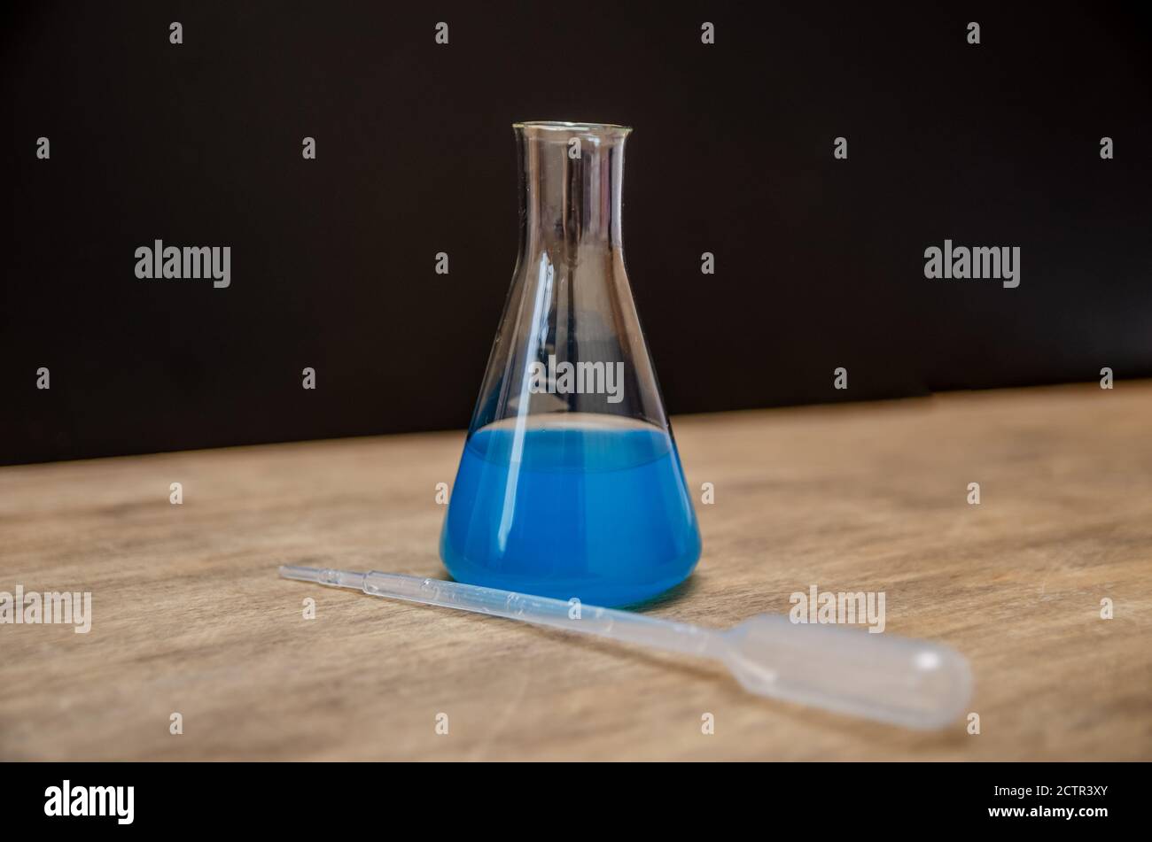 Chemical flask with blue laboratory dyes inside on a black background ...