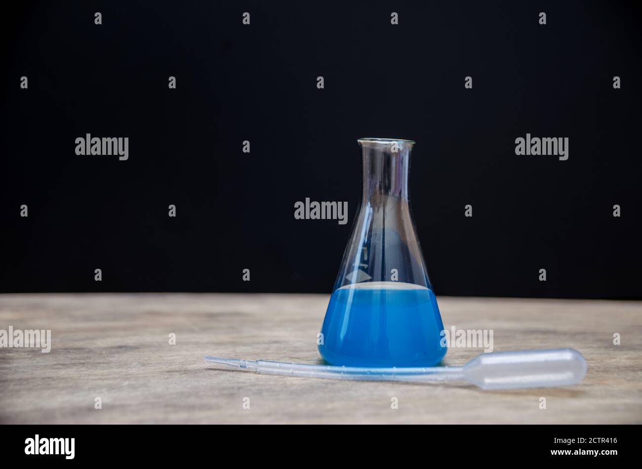 Chemical flask with blue laboratory dyes inside on a black background ...