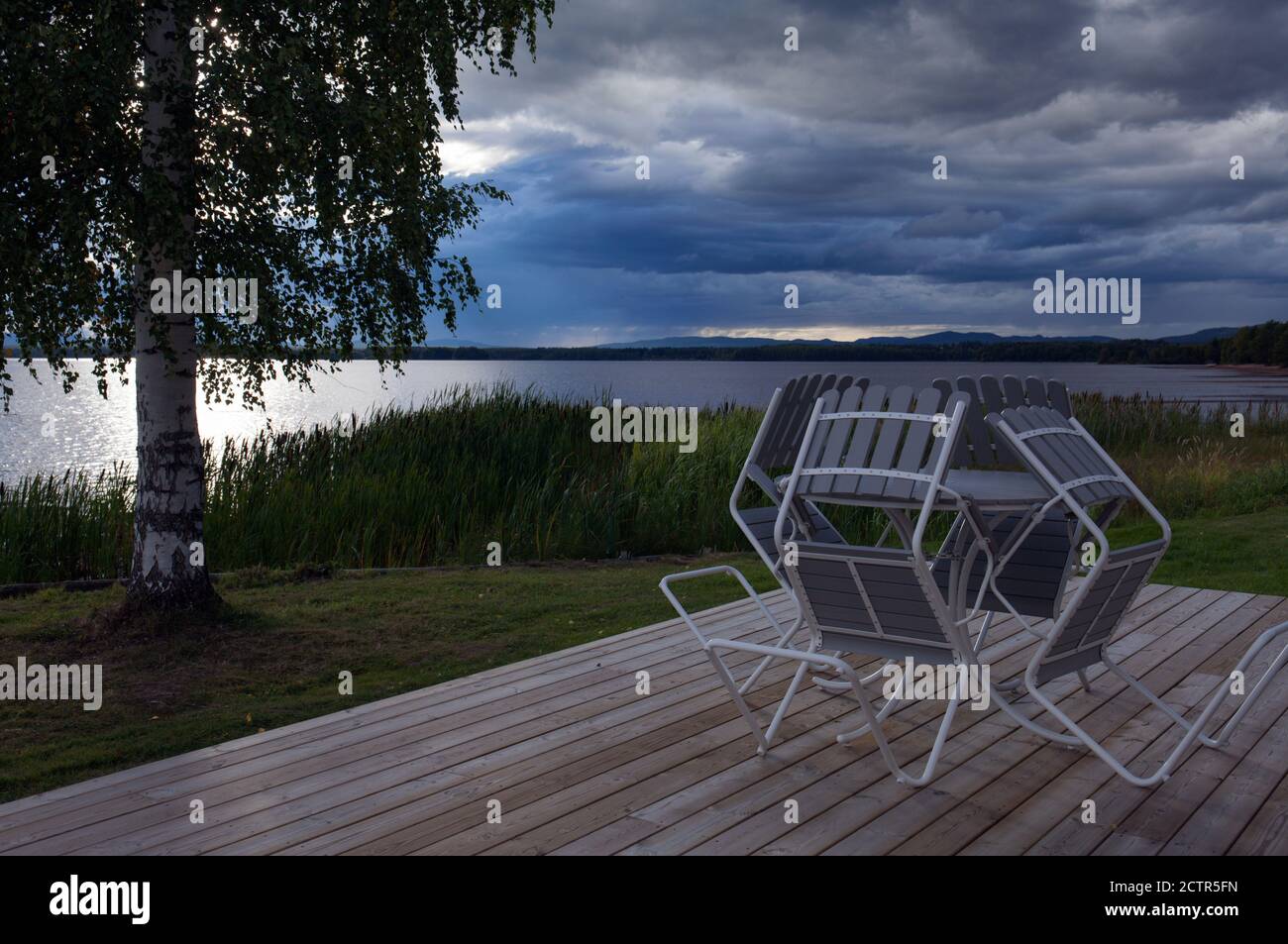 View from a deck towards lakeshore and lake. Chairs and table on the ...