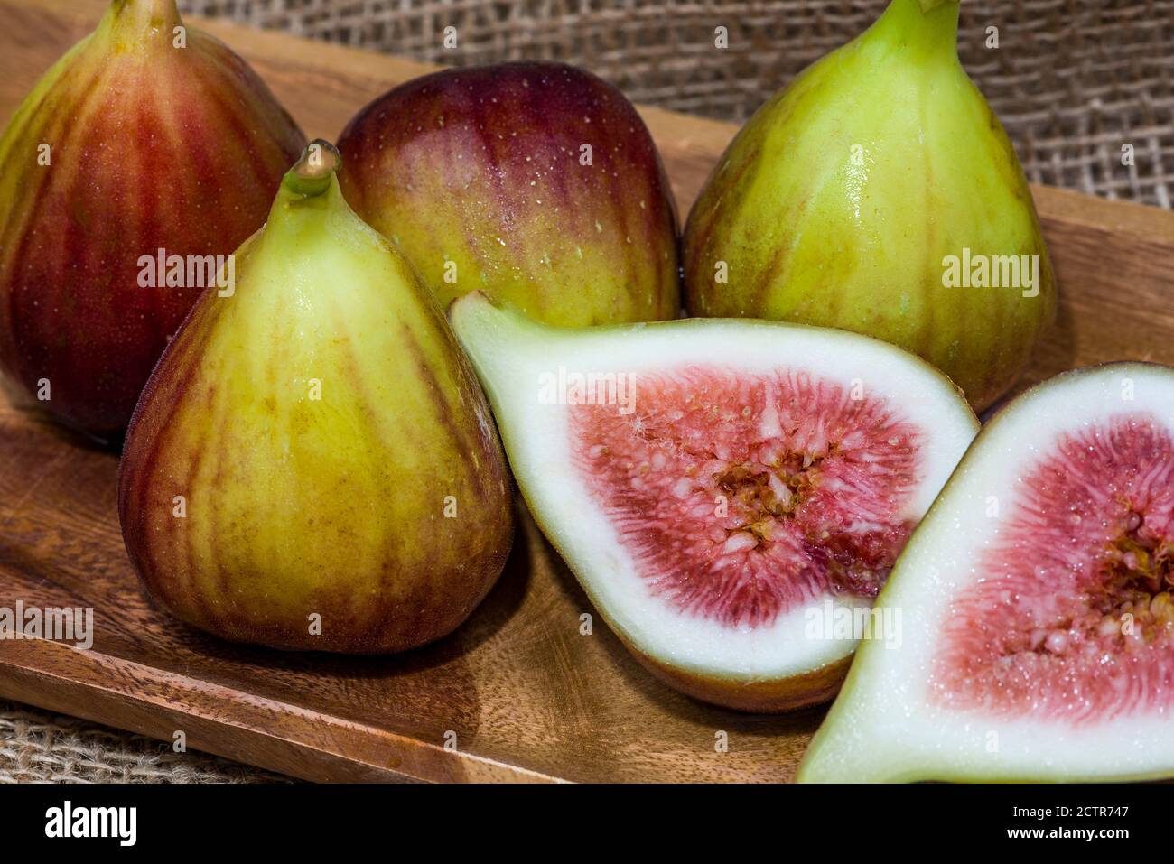 Fresh fig sliced in half with whole figs in the background, on a wooden ...