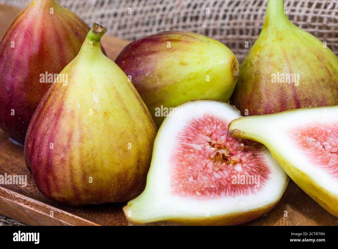Fresh fig sliced in half with whole figs in the background, on a wooden ...