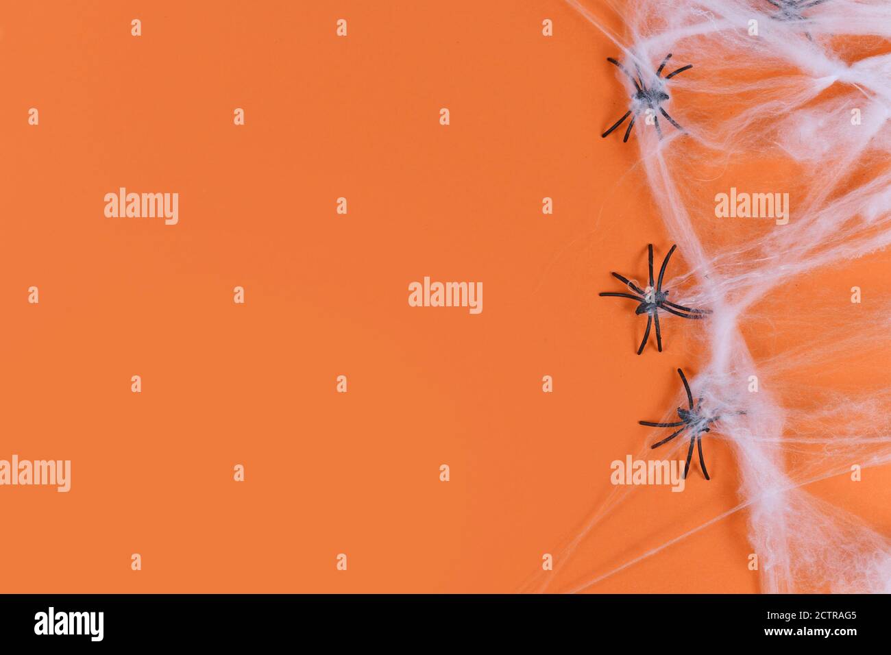 Spider webs and plastic spiders on side of orange Halloween background ...