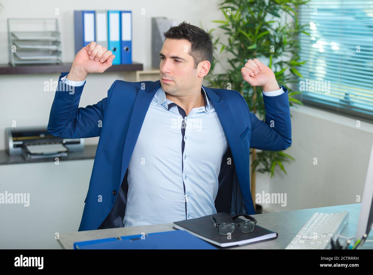 businessman having a stretch while sat at office desk Stock Photo - Alamy