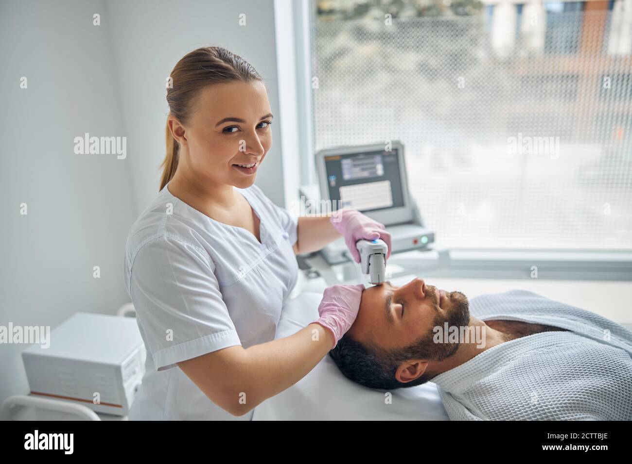 Smiling cosmetologist treating male skin with laser device Stock Photo ...