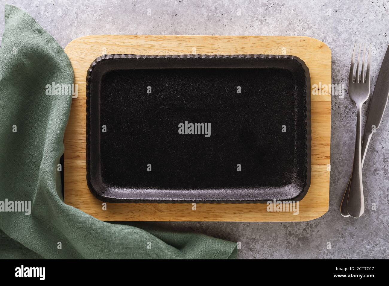 Cast iron tray with stand and cutlery on the table, top view. Food ...