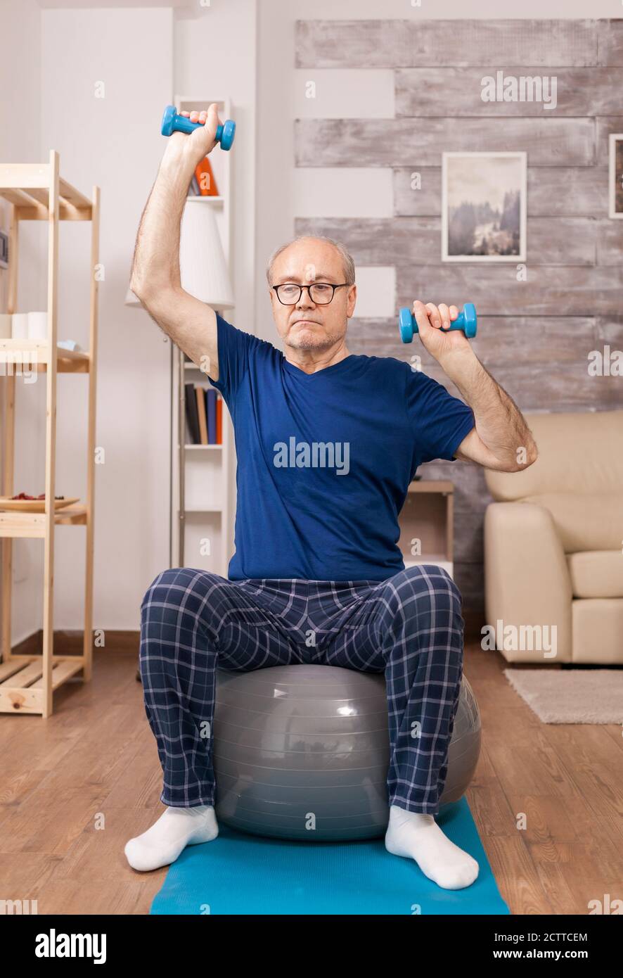 Elderly man doing sport in pajamas using dumbbells. Old person ...