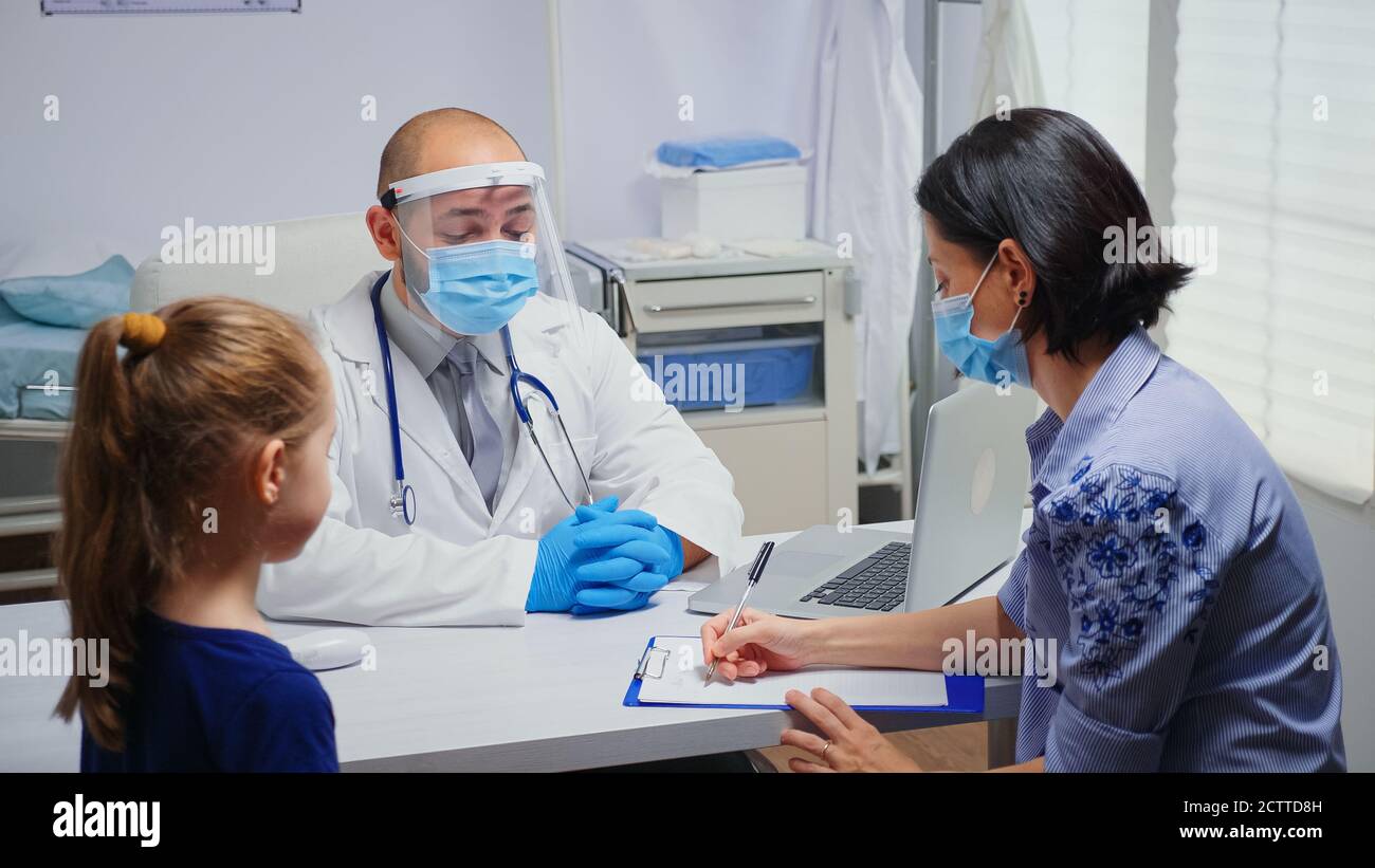 Mother writing on clipboard doctor instructions wearing protection mask ...