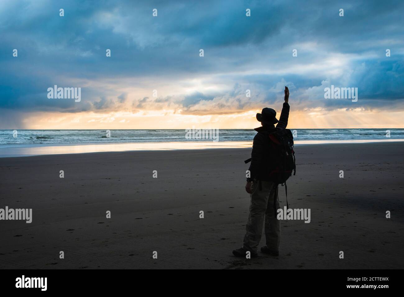 Silhouette image of a man with one arm up standing on the beach facing ...