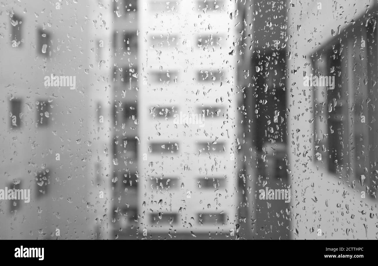 Closeup the rain drops on window's glass with blurry modern buildings ...