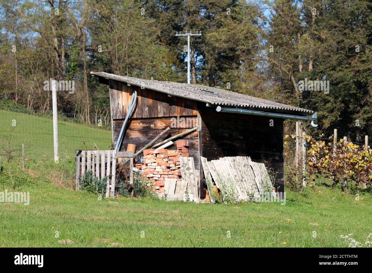 Old wooden boards garden tool shed covered with dilapidated roof tiles surrounded with building ...