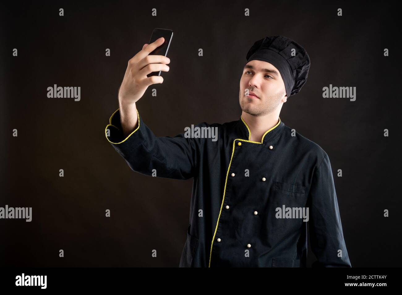 Portrait of young male dressed in a black chef suit taking selfie ...