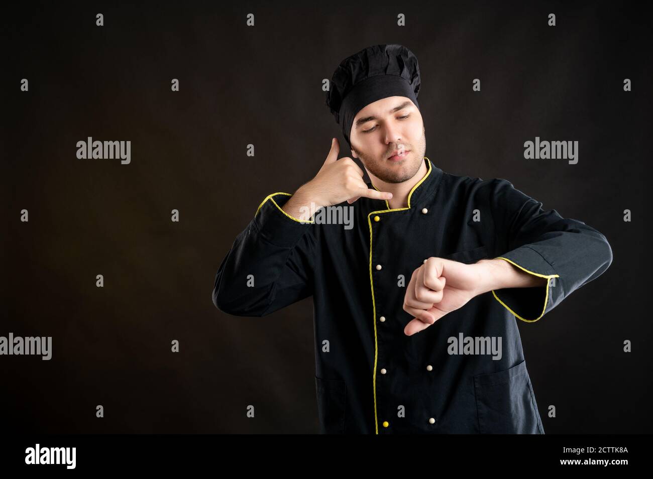 Portrait of young male dressed in a black chef suit showing it's time ...