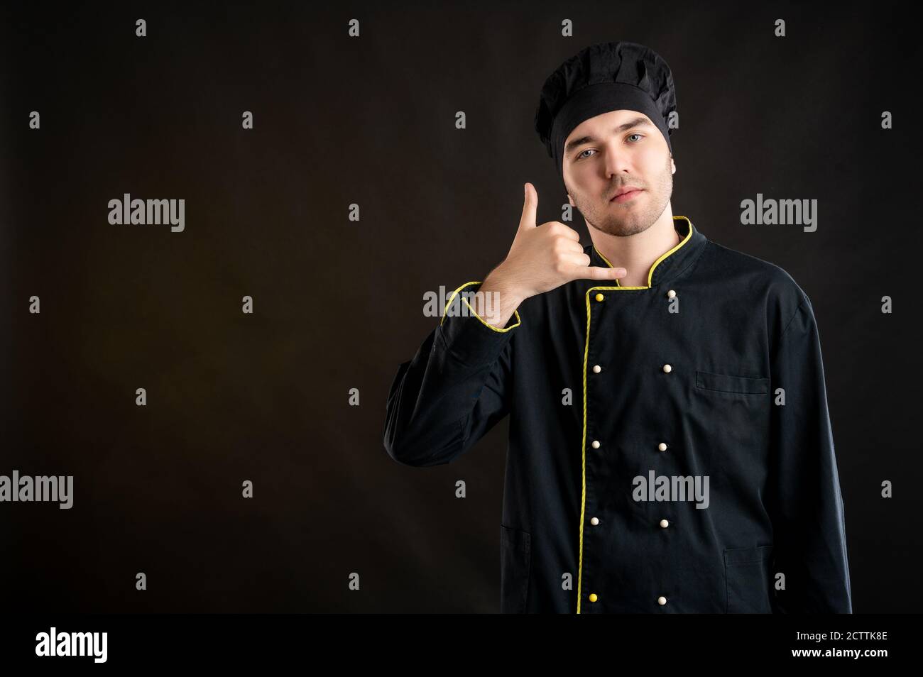 Portrait of young male dressed in a black chef suit showing call me ...