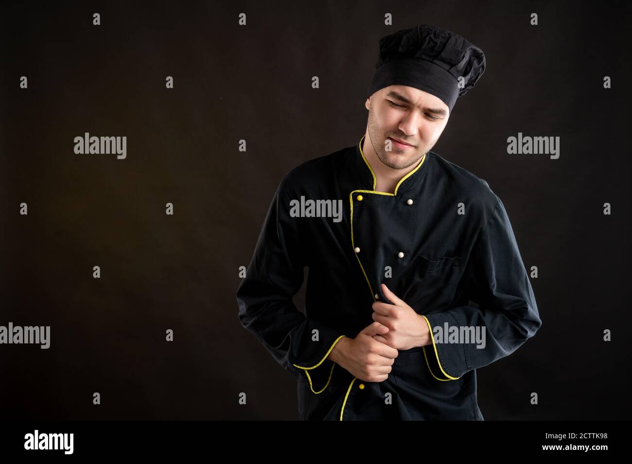 Portrait of young male dressed in a black chef suit has stomach pain ...