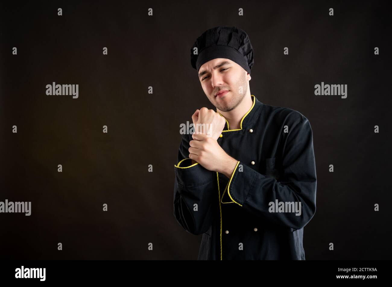 Portrait of young male dressed in a black chef suit has wrist pain ...