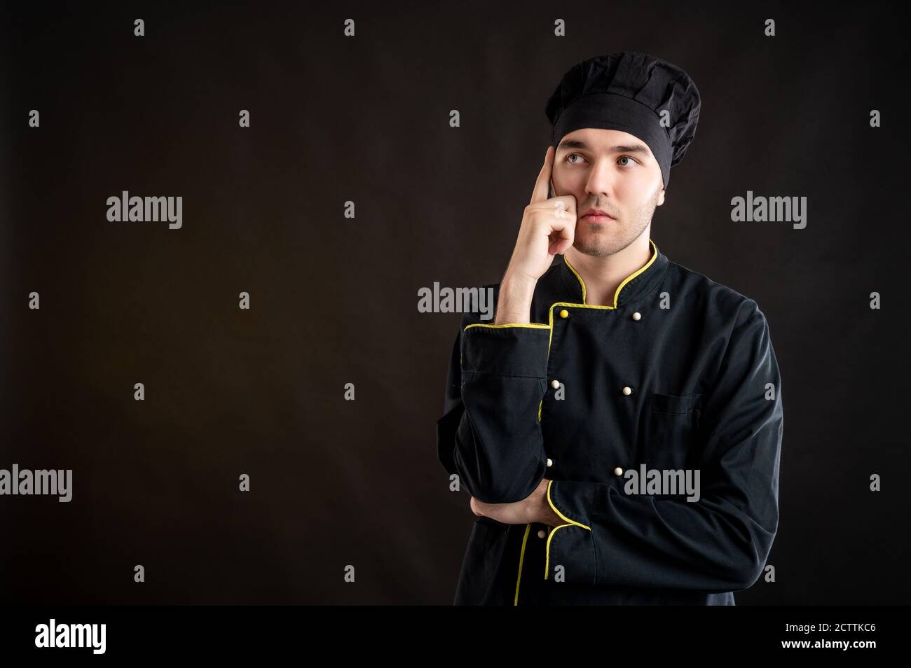 Portrait of young male dressed in a black chef suit wondering posing on ...