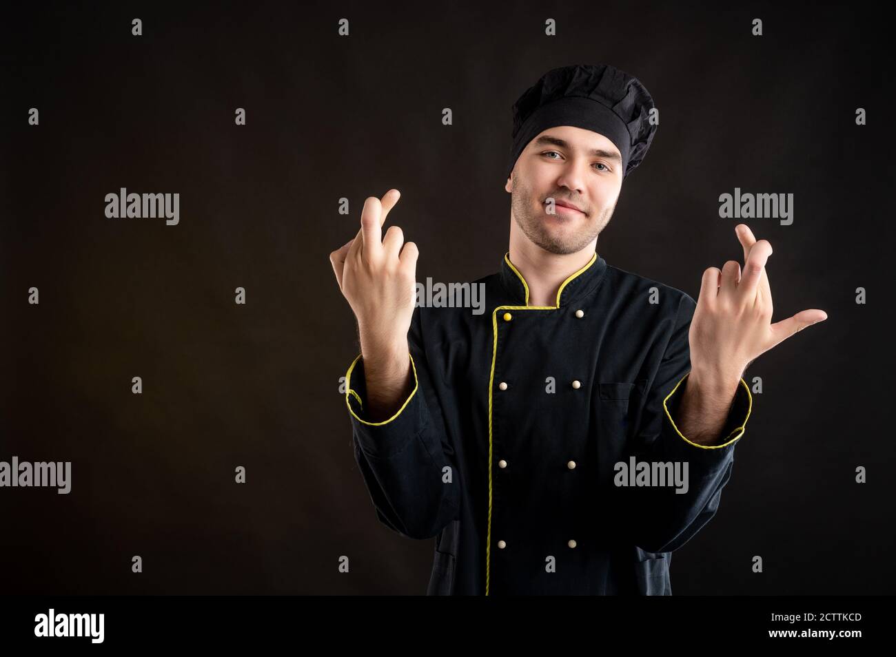 Portrait of young male dressed in a black chef suit showing double good ...