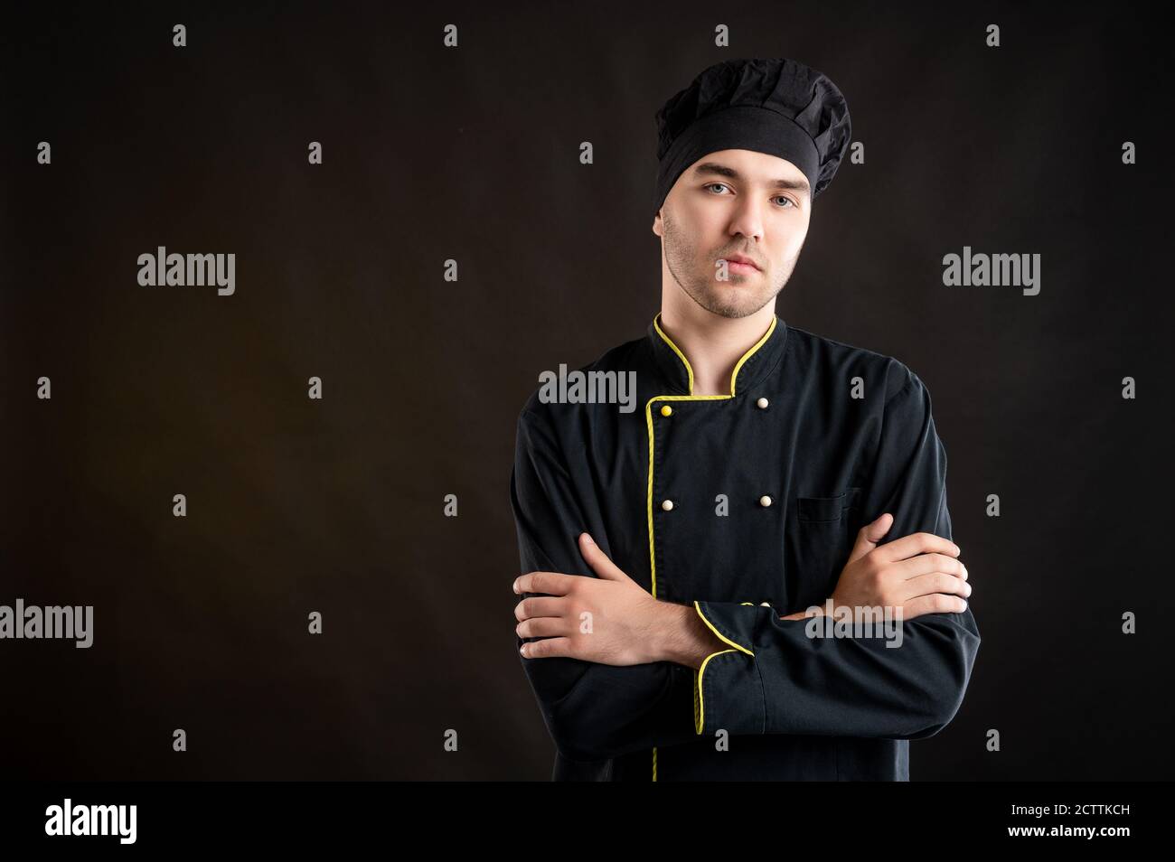 Portrait of young male dressed in a black chef suit looking confident ...