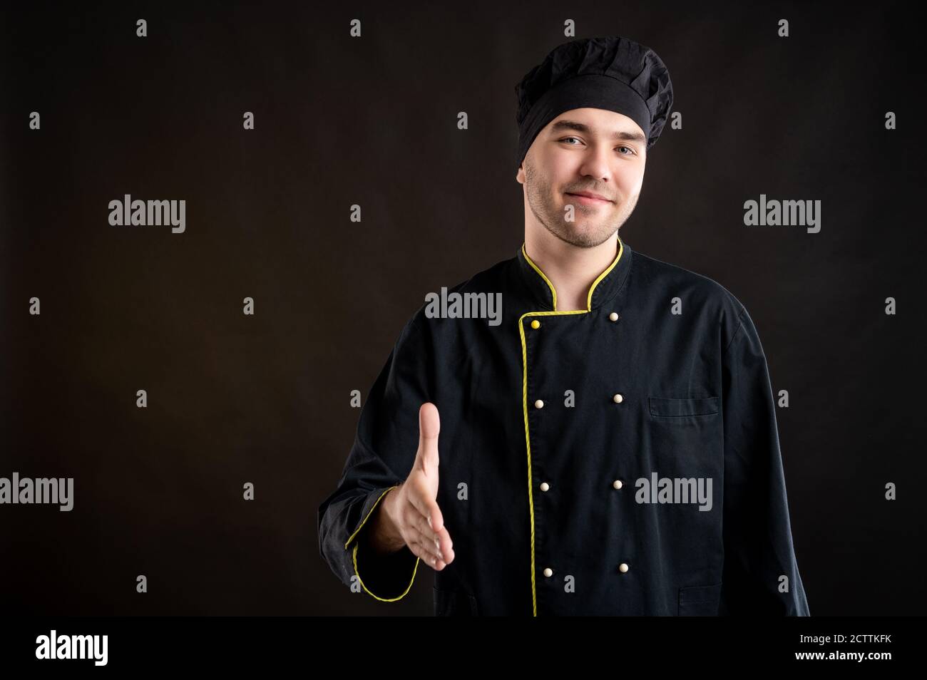 Portrait of young male dressed in a black chef suit shaking hand posing ...