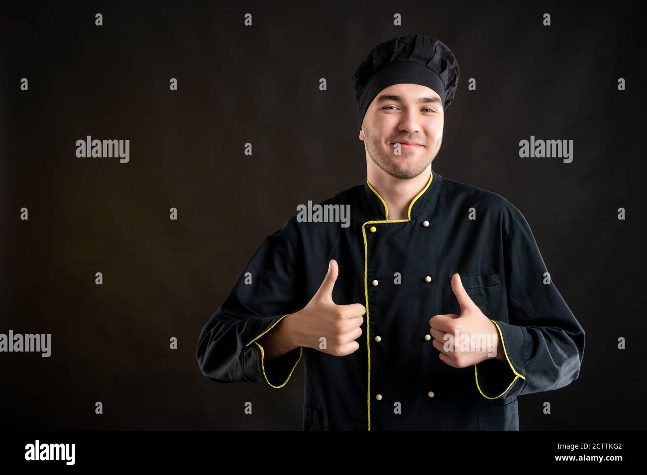 Portrait of young male dressed in a black chef suit showing thumbs up ...