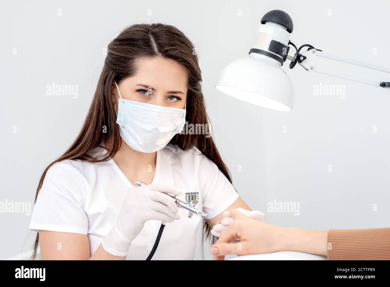 Portrait of manicure master uses airbrush wearing mask in nail salon ...