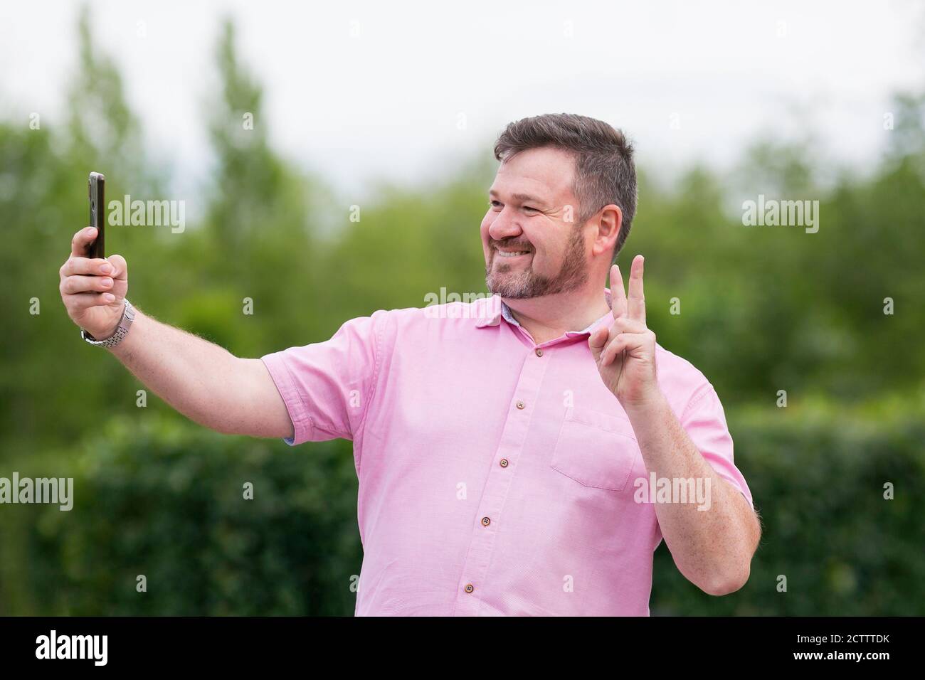 Cheerful fat man with a beard takes pictures of himself on a smartphone ...