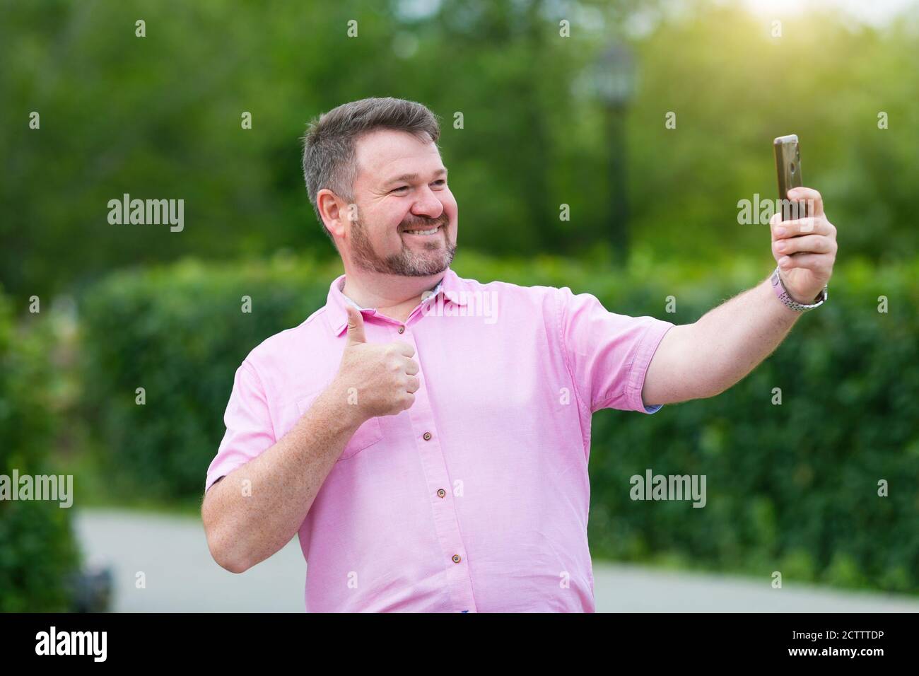 Cheerful fat man with a beard takes pictures of himself on a smartphone ...