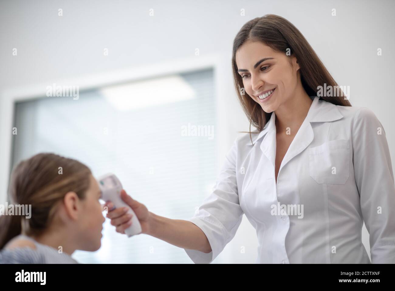 Dark-haired smiling doctor checking temperature of her small patient ...