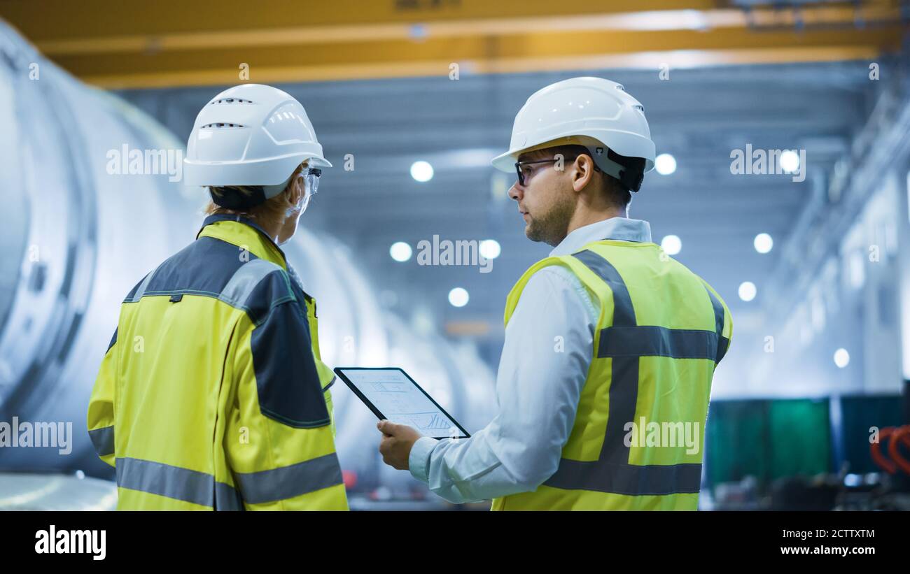 Two Heavy Industry Engineers Stand in Pipe Manufacturing Factory, Use ...